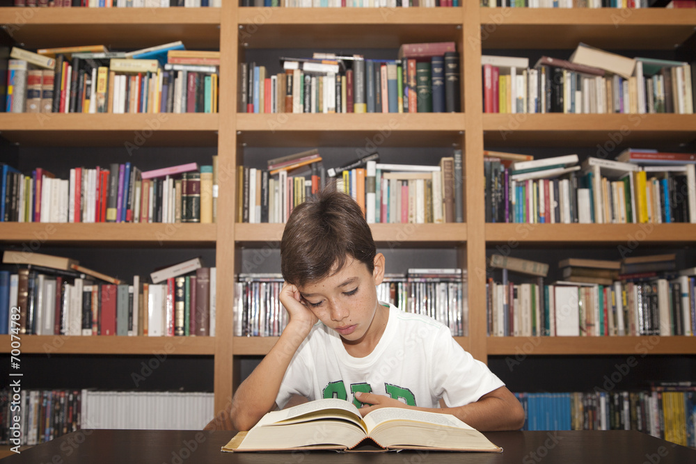Foto de Stock Niño leyendo libro junto a librería | Adobe Stock