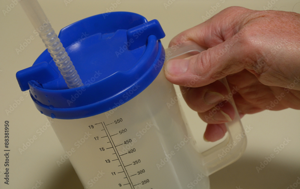 Hand holding plastic hospital cup of water with straw and lid and ...