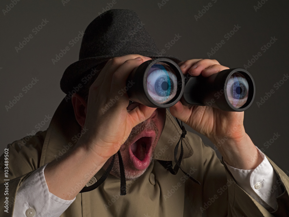 Photograph of a man in trench coat and hat looking through binoculars ...