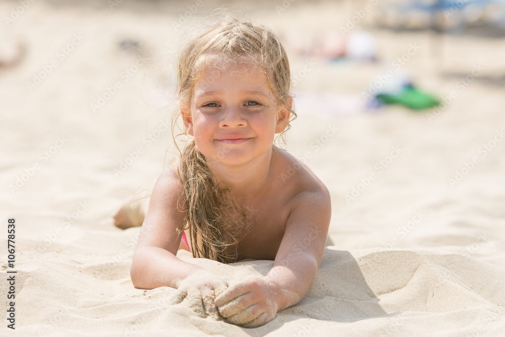 Pretty girls four years lying in the sand on his stomach on the beach ...