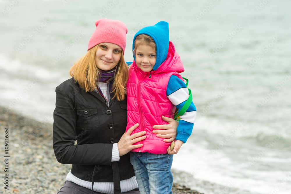 Mom and daughter in warm clothes hugging each other on the beach in ...