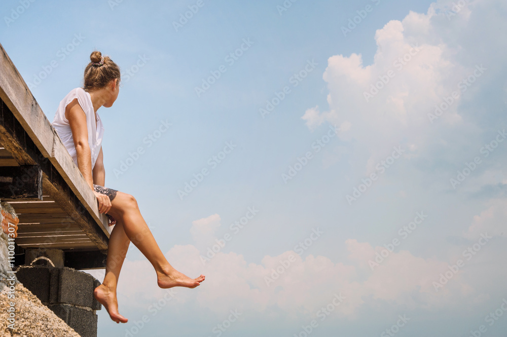 Young woman sitting on the wooden platform edge and swinging her legs ...