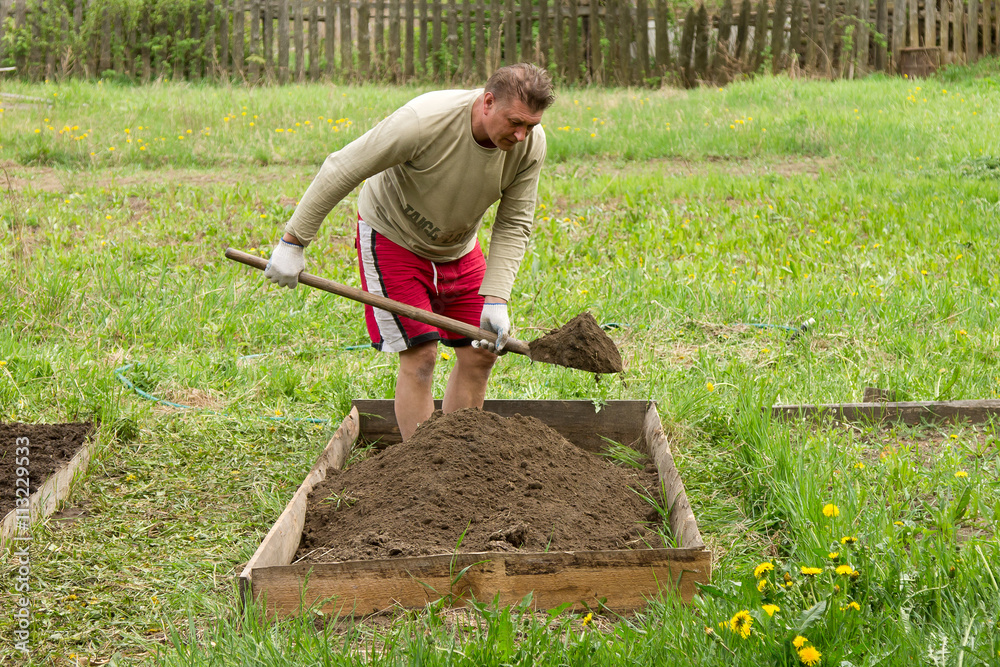 Man digging up a garden-bed to garden plants on a countryside. Man with ...