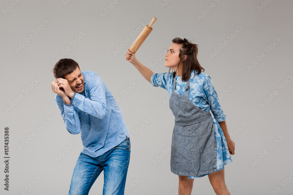 Young woman beating man with rolling pin over grey background. の Stock ...