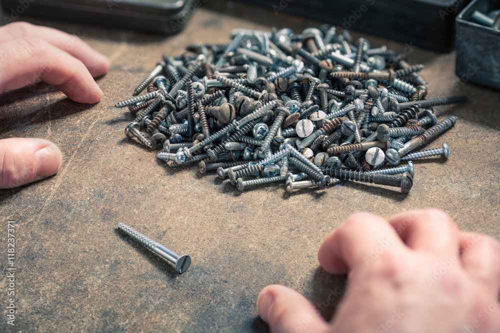 Pair of hands, one screw standing out from pile of different sized ...
