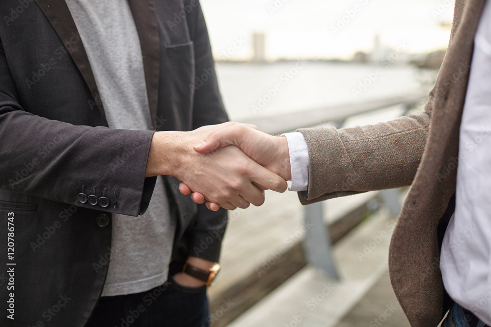 Mid section view of two businessmen shaking hands on waterfront, London ...