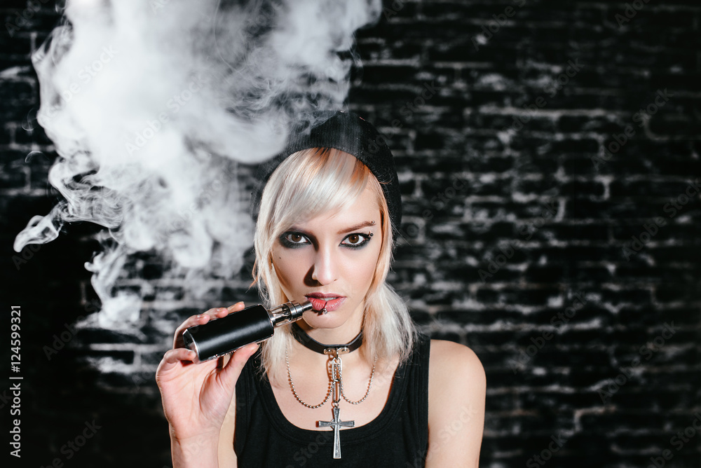 Sexy goth girl smokes electronic cigarette on dark background. The ...