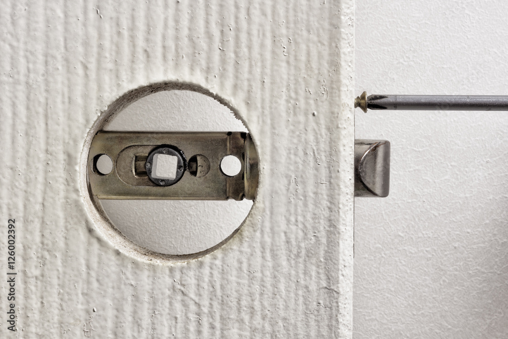 Install door latch with a screwdriver. Stock Photo | Adobe Stock