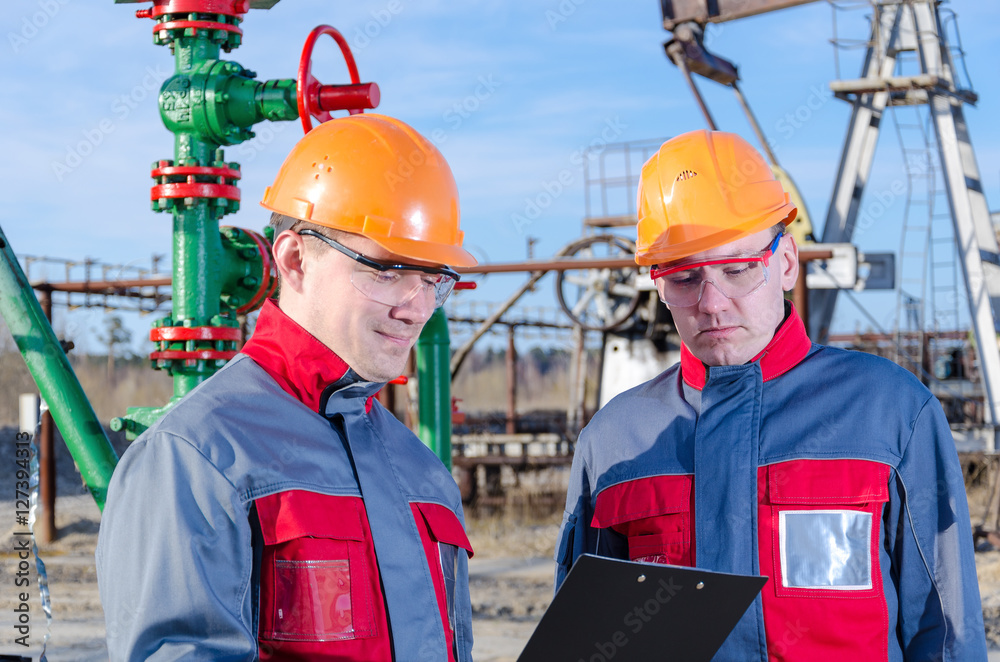 Two workers in the oilfield checking test results. Pump jack and ...