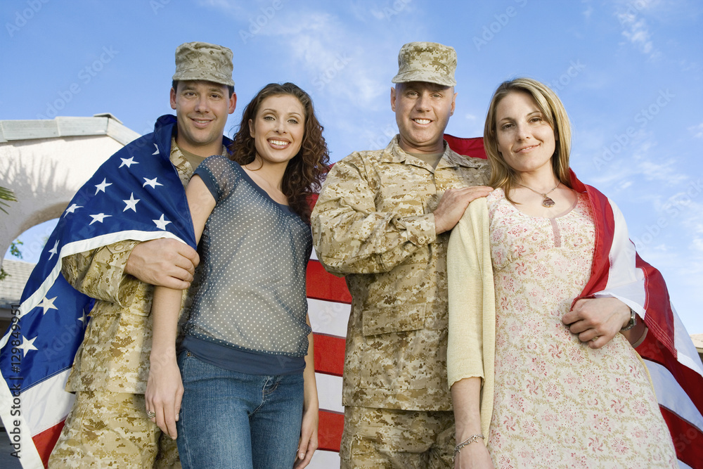 Low angle portrait of happy military couples wrapped in American flag ...