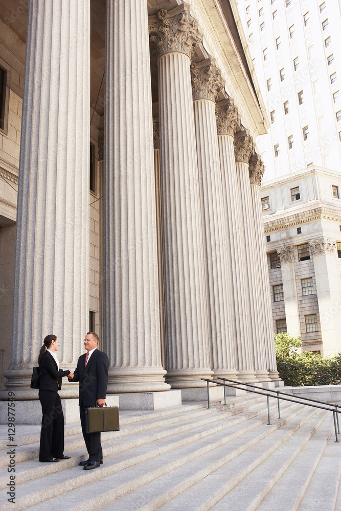 Full length side view of male and female attorneys shaking hands on ...