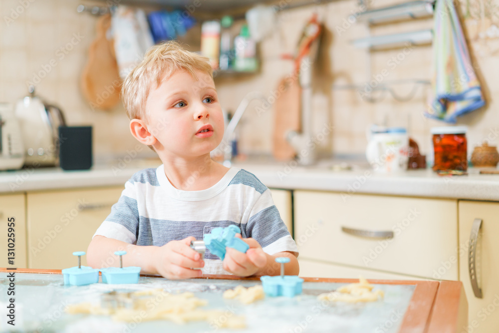 Little blond kid plays with molds for making ginger biscuits or cookies ...