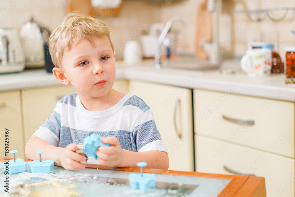 Little blond kid plays with molds for making ginger biscuits or cookies ...