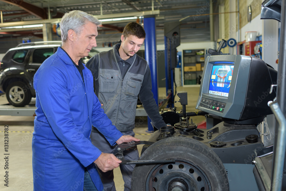 apprentice mechanic and teacher retreading wheel in automotive workshop ...
