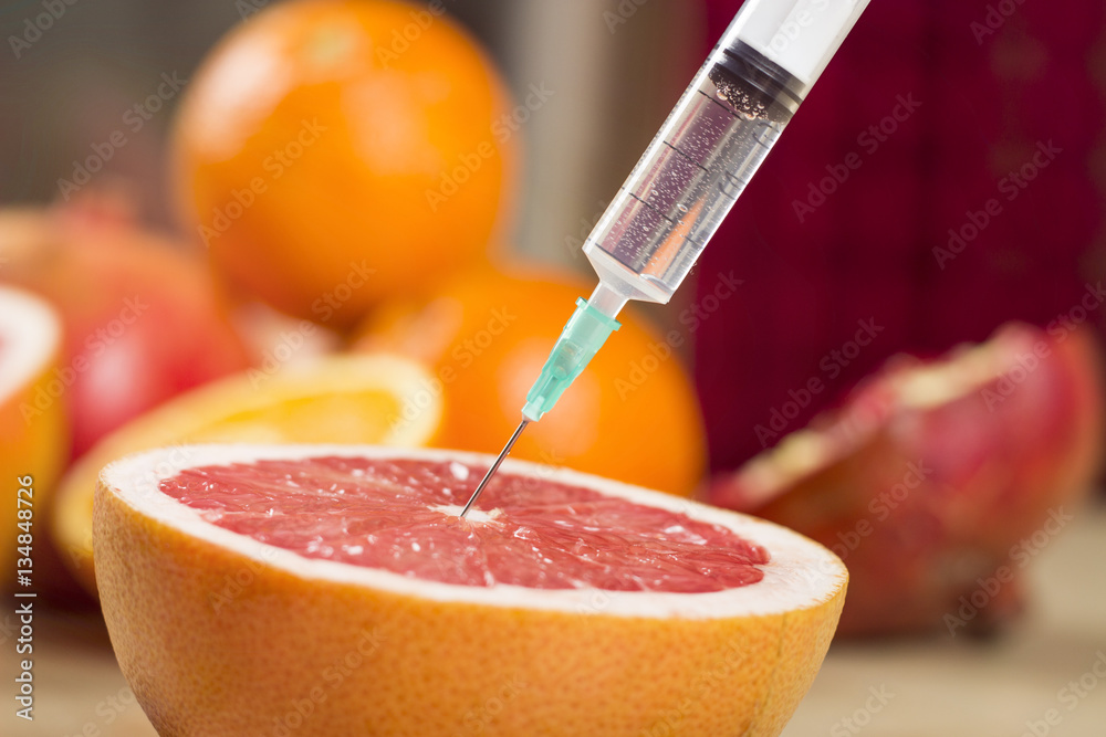 Needle and syringe injected in the fruit. Nutrition concept. Enhanced ...