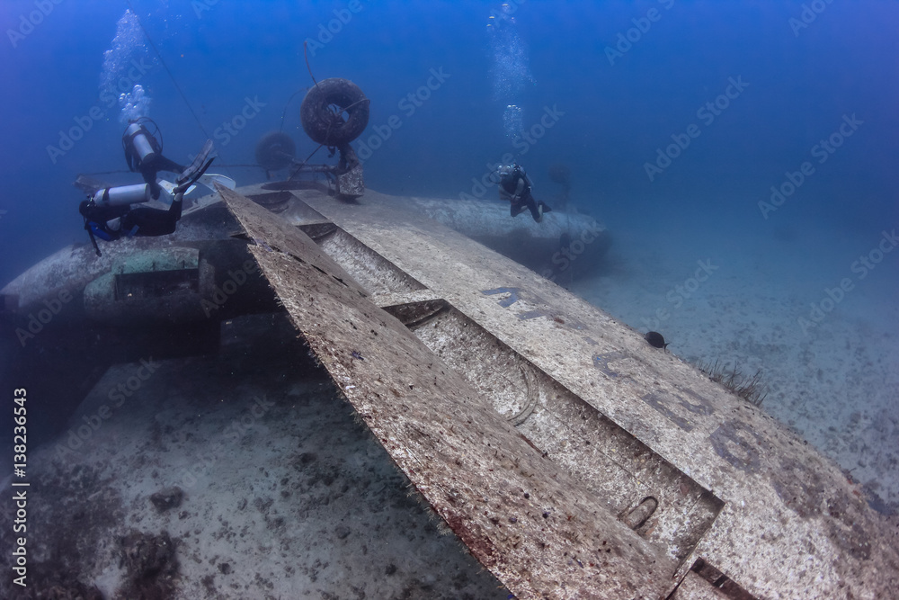 SCUBA divers over the wing of an upside down aircraft wreck on the ...