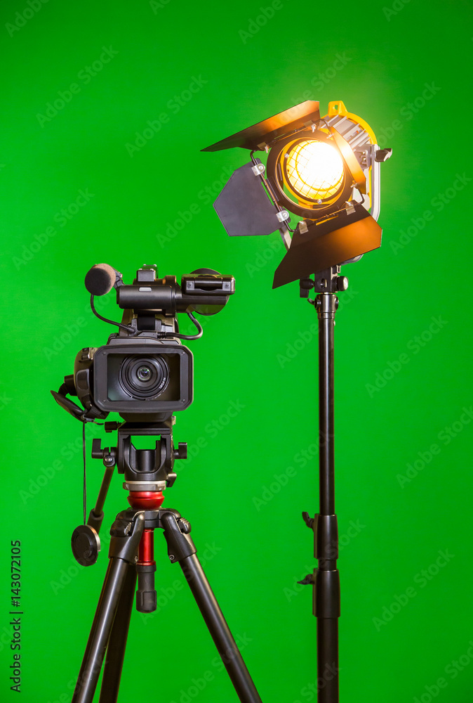 A video camera and a spotlight with a Fresnel lens on a green ...