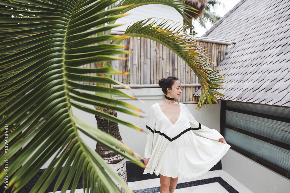 Woman in white tunic in tropical garden with palm tree and white ...