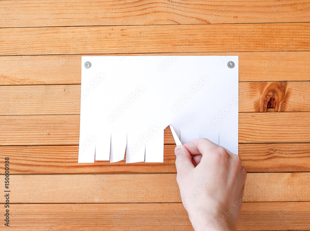 Hand pulls a piece of paper. Empty paper ad loose leaves on a wooden ...