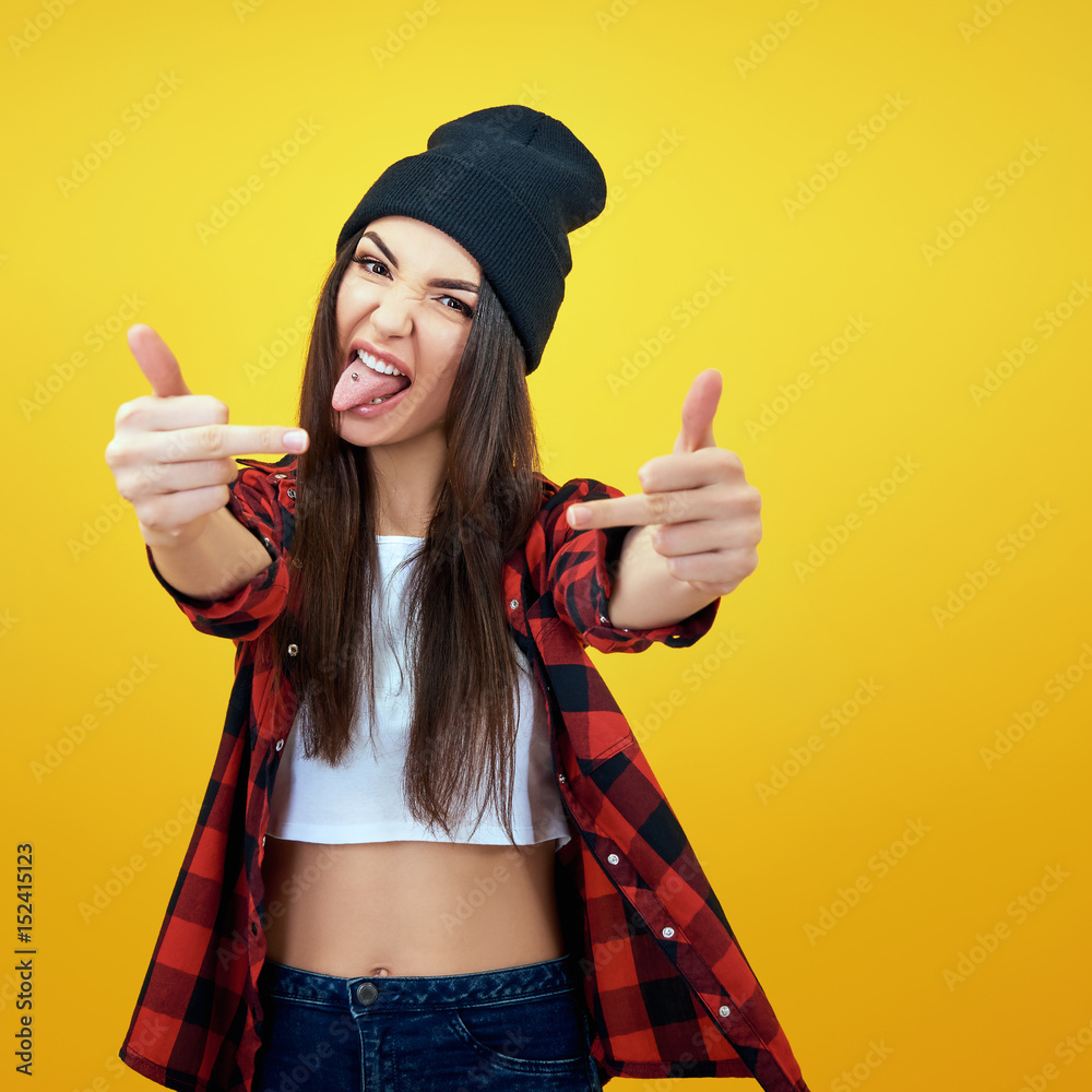 Hipster girl in jeans, checked shirt and hat showing middle fingers ...
