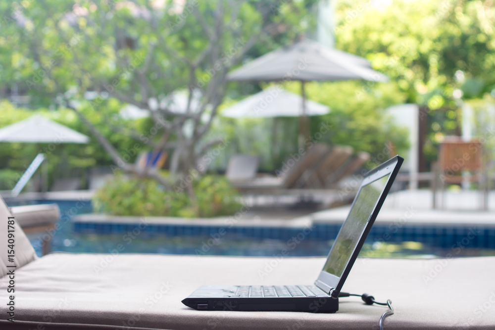 side view of laptop on the deckchair in swimming pool side. computer ...