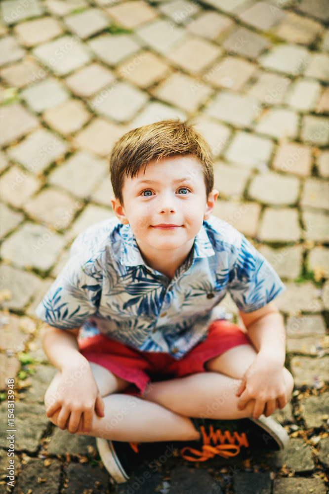 Candid portrait of adorable kid boy sitting on the floor looking at the ...