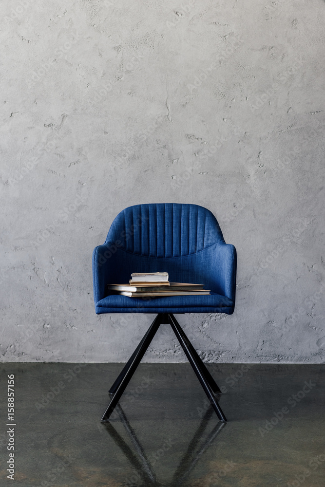 Modern blue chair with books standing in empty room with grey wall ...