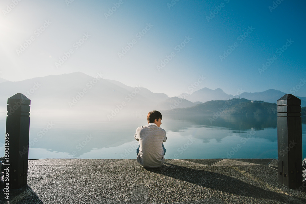 Lonely Asian man sitting alone on a public pier on a clear lake in an ...