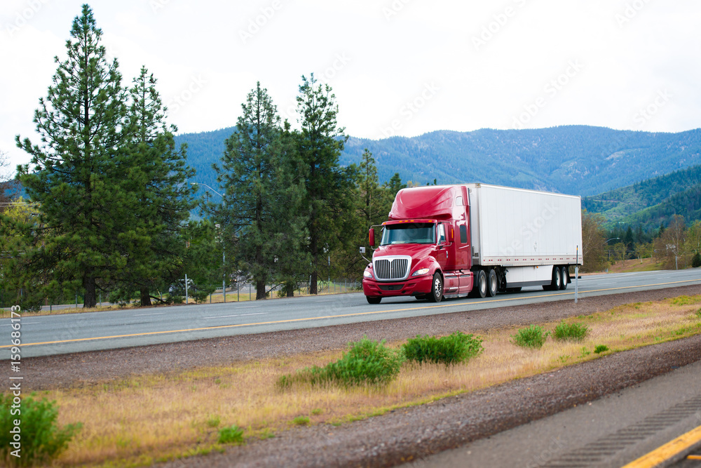 Red modern semi truck with dry van trailer moving by divided highway I ...
