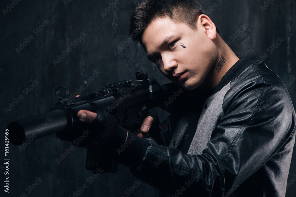 Sniper with tattoo on face and rifle close-up. Armed asian killer man ...
