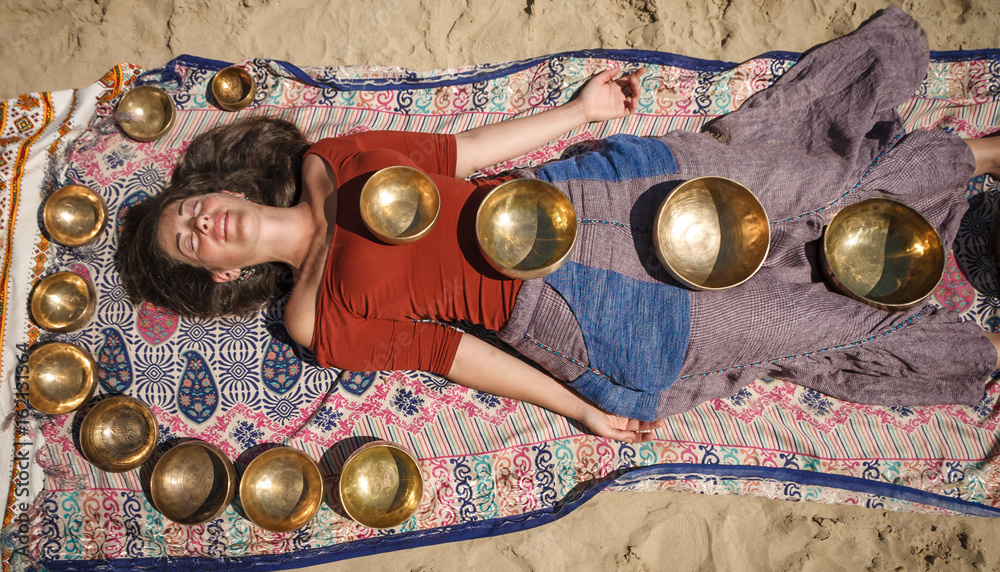 Beautiful female receiving energy sound massage with singing bowls on ...