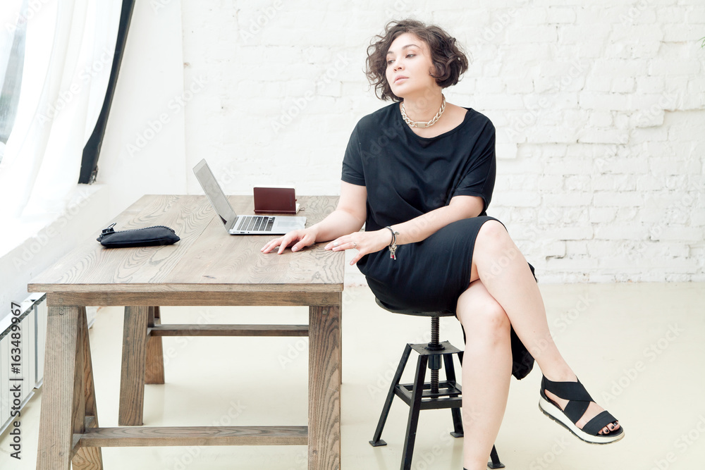 Young plus size female model sitting in front of the table and working ...