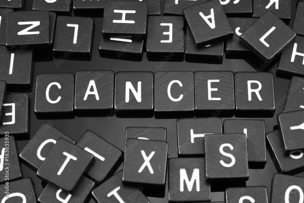 Black letter tiles spelling the word "cancer" on a reflective ...