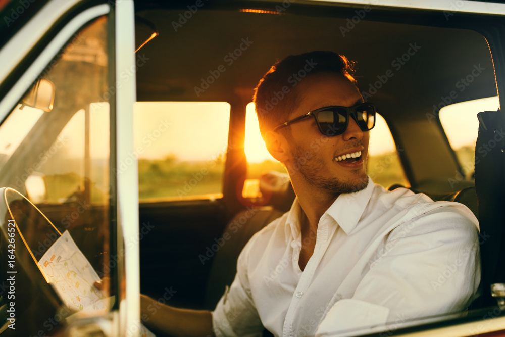 Handsome happy young man with a map in the car. Smiling man using map ...