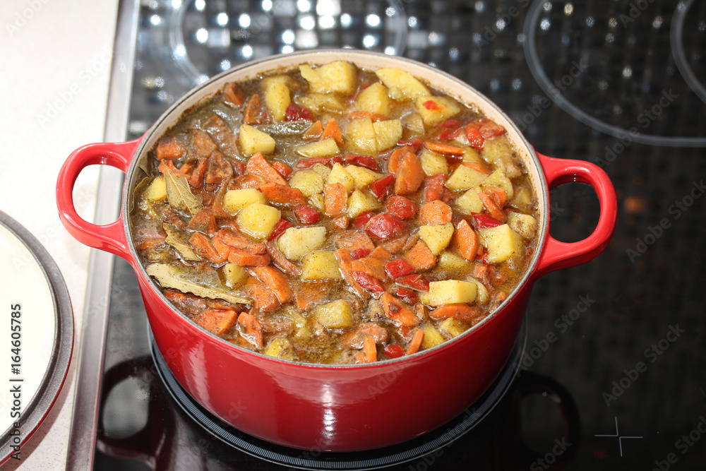 Cooking. Beef stew with potatoes, pepper and carrots in big red round ...