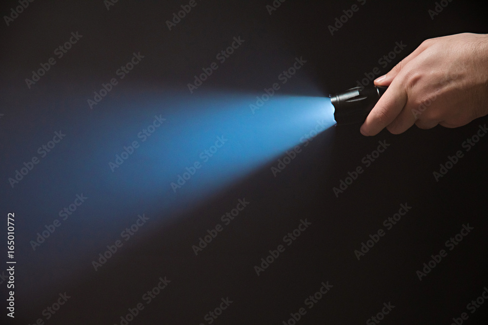 Male hand holding a led flashlight with a narrow blue beam on a black ...