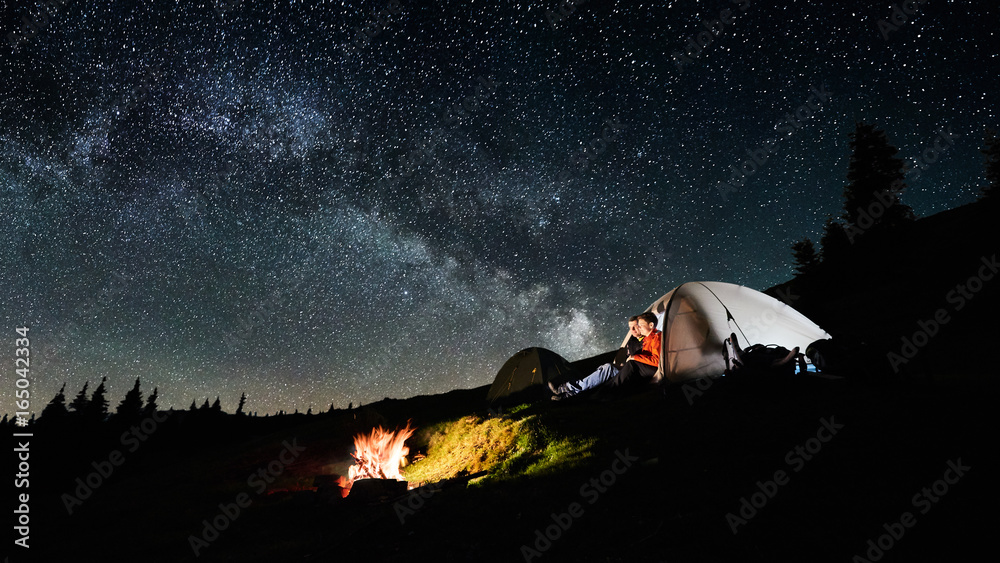Fotografie Night camping. Man and woman tourists sitting in the ...