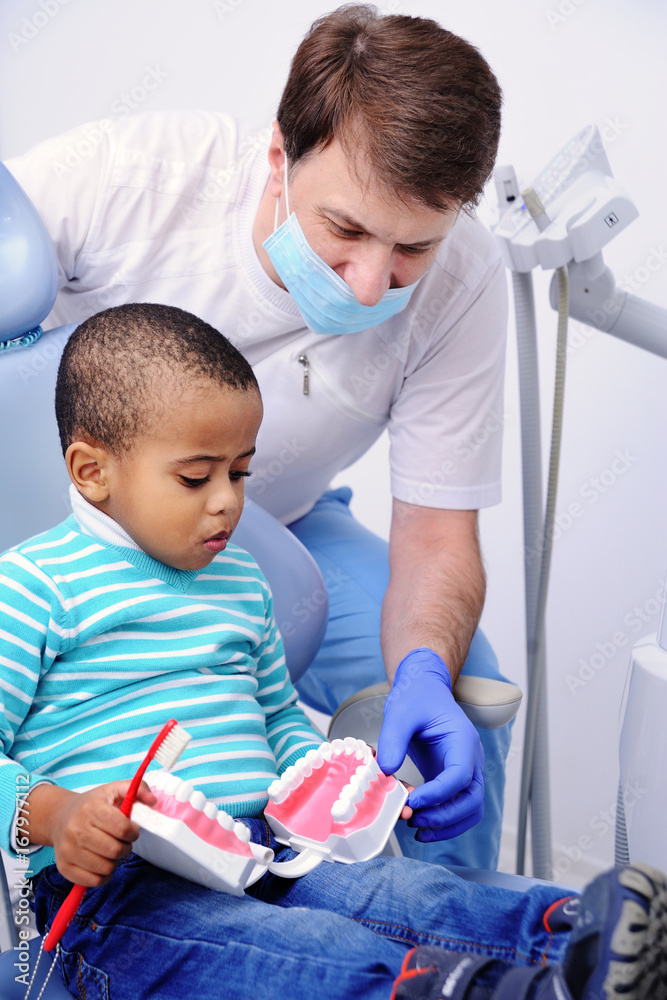 pediatric dentist man shows African boy with dark skin how to properly ...