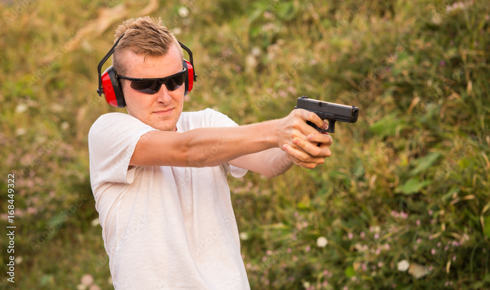 Young blonde handsome guy shooting from fire arms gun violent pistol ...