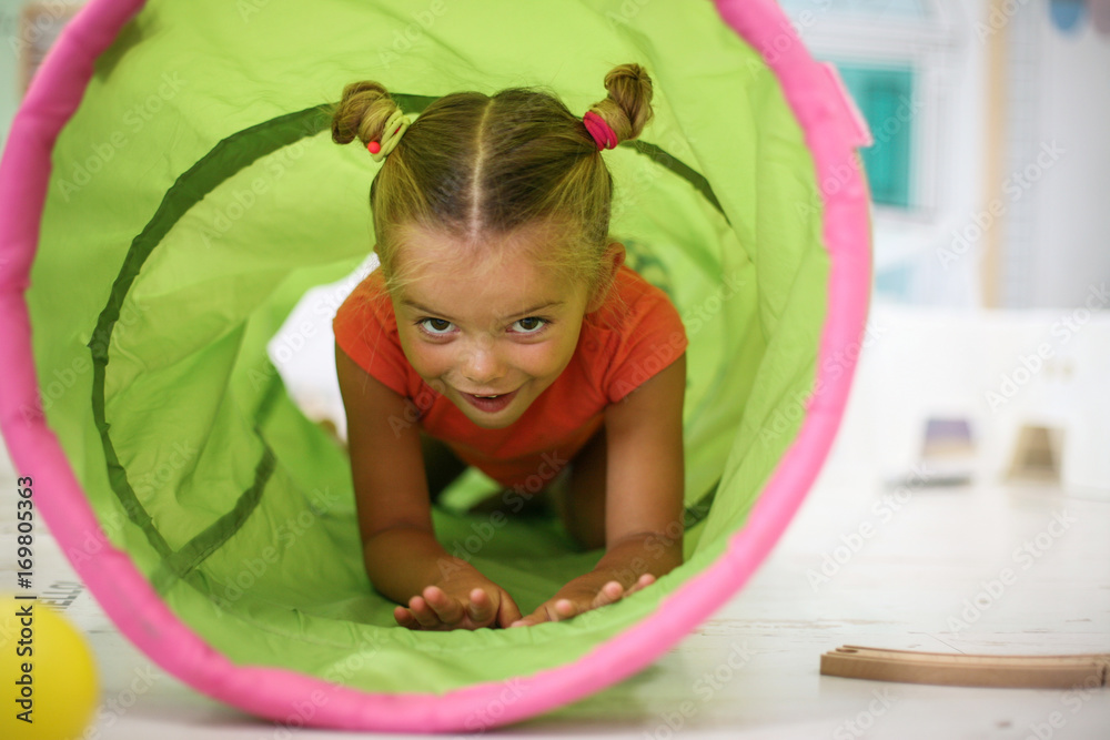 A little girl in playground. The little girl runs through the tunnel ...