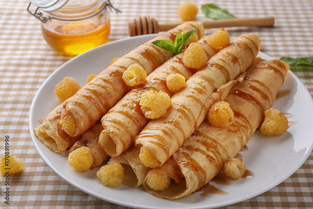 Rolled thin pancakes served with yellow raspberry and honey on white ...