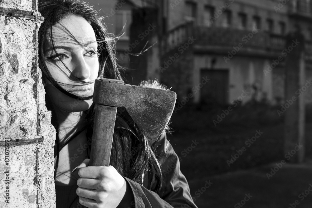 Woman escaping from someone, defending herself with an axe, outdoors ...
