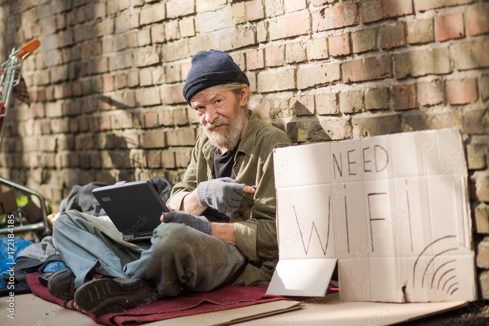 Homeless man pointing on cardboard with sign need wi fi. Tramp sitting ...