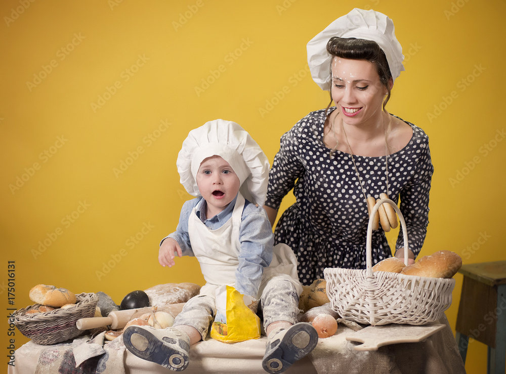 Mother and son in the costume of the chefs playing with flour on yellow ...