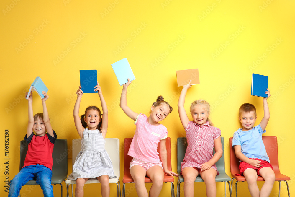 Cute little children with books sitting near color wall Stock Photo ...