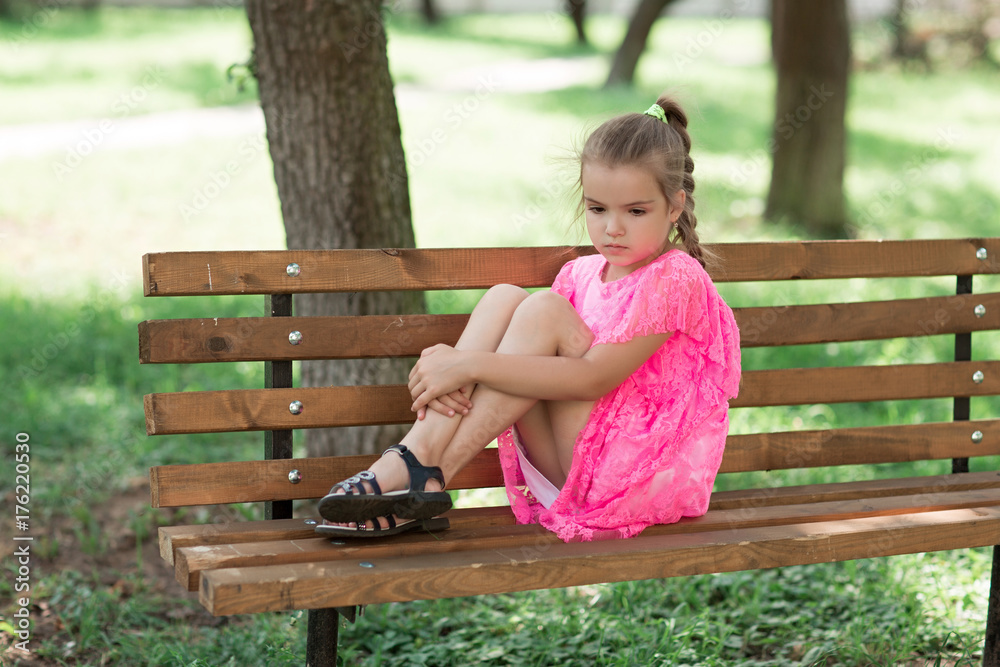 Fotografie Little caucasian girl sitting in park on bench. A child in a ...