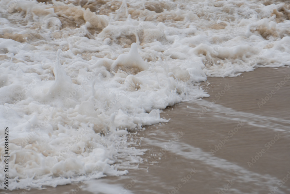 Ocean waves crash on a sandy beach in day time. Rip current pull water ...