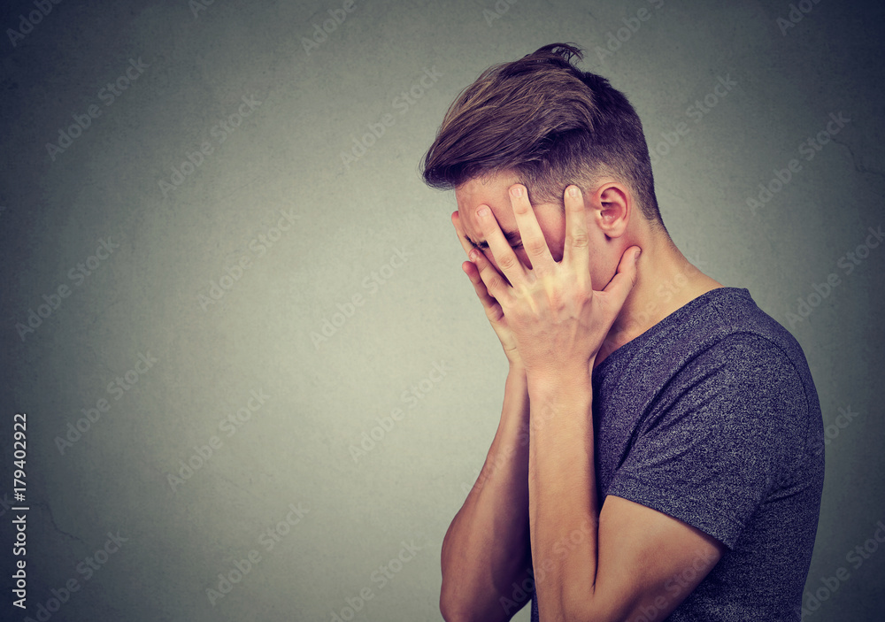 Side profile of a sad young man with hands on face looking down ...