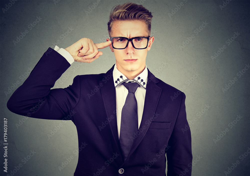 Angry young man gesturing with his finger against temple asking are you ...