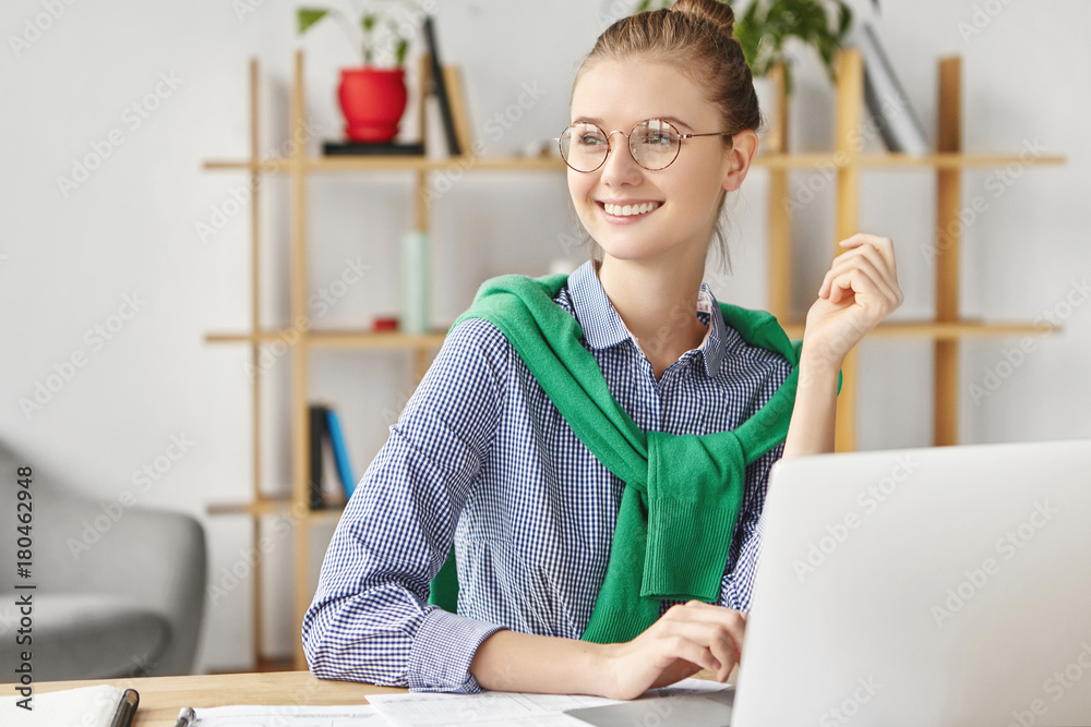 Dreamful cheerful positive glad female model poses in office at work ...